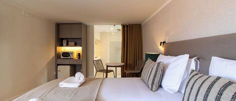 Quarto de hotel com duas camas, uma kitchenette pequena, uma mesa de jantar e um espaço de estar separado.