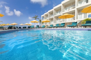 Piscina com espreguiçadeiras e guarda-sóis, rodeada por um edifício de vários andares com varandas.