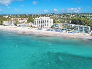 Um hotel à beira-mar com vários edifícios, uma praia de areia e um mar azul cristalino.