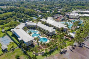 Um resort com várias piscinas, quadra de tênis e vegetação exuberante.