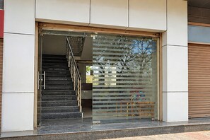 Entrada de um edifício com porta de vidro, escadas de metal e vista para o exterior.