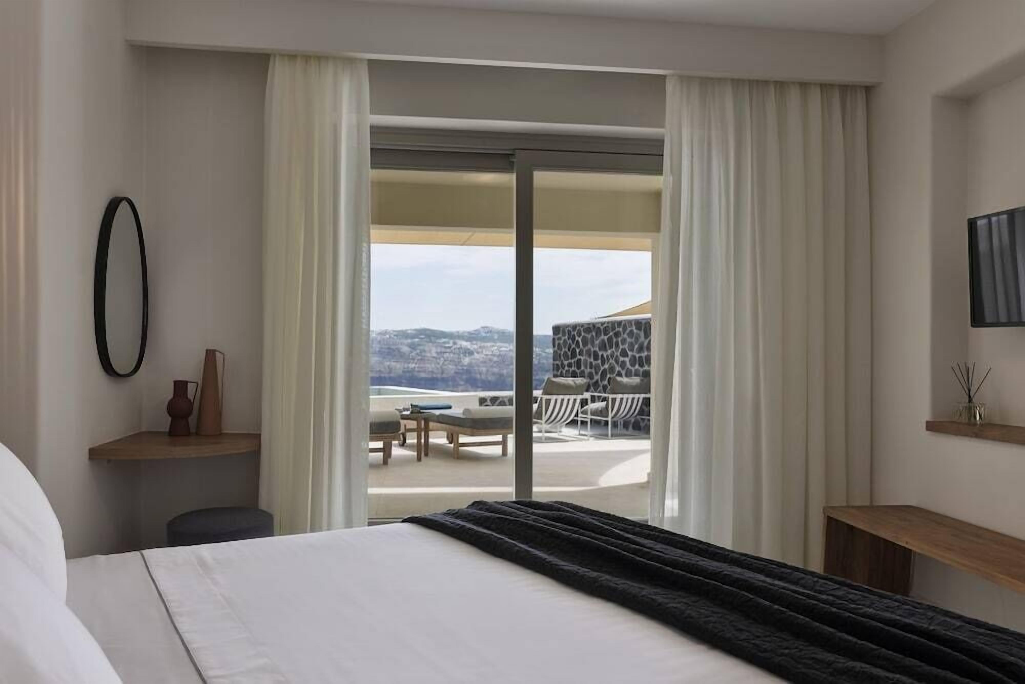 Quarto de hotel com cama, escrivaninha, cadeira, mesinha e vista para o exterior.
