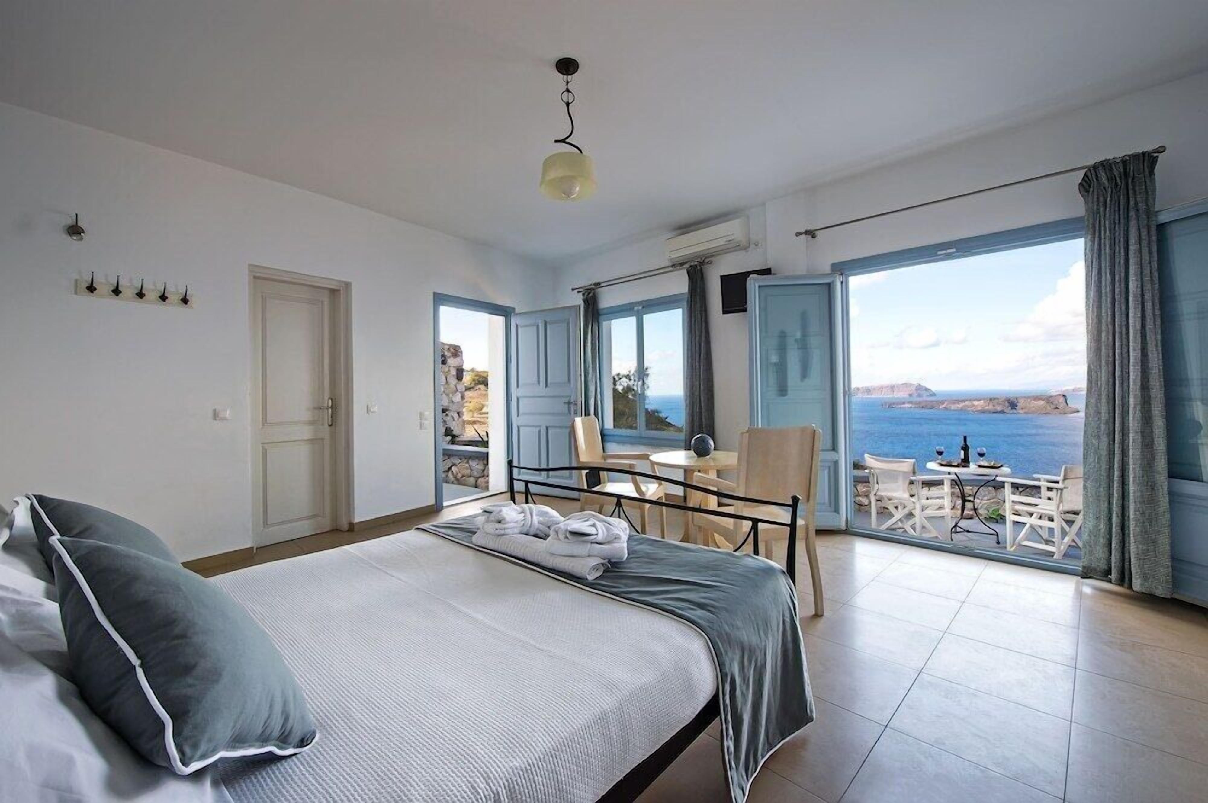 Um quarto com uma cama, uma mesa e vista para o mar.