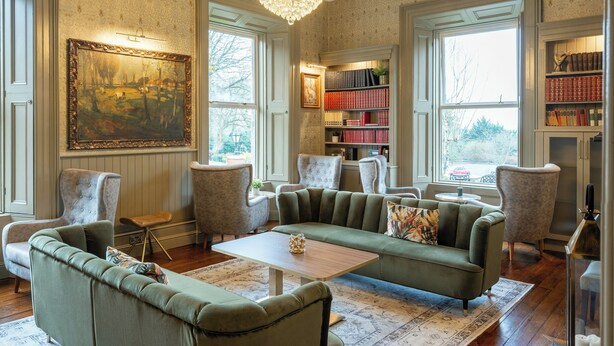 Quarto com sofá verde, poltronas, mesa de centro de madeira e estante repleta de livros.