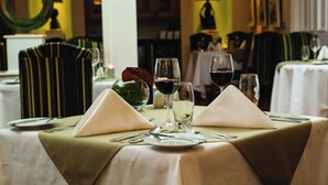 Mesa de restaurante posta com toalha verde, guardanapos brancos e copos de vinho.