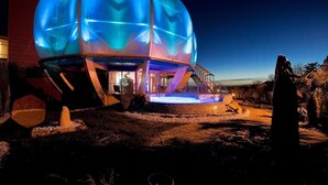 Uma estrutura esférica com uma cúpula transparente, iluminada por dentro, e uma escadaria que leva a uma entrada.