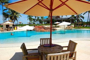 Uma área de piscina com mesa e cadeiras de madeira, guarda-sóis e espreguiçadeiras.