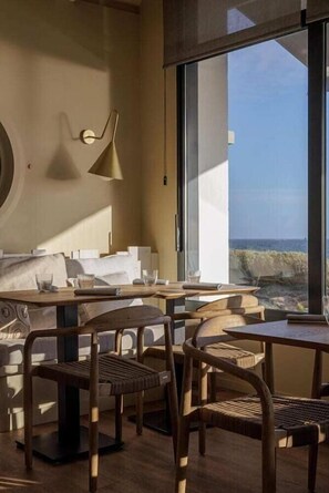 Interior moderno com área de jantar, móveis de madeira e uma grande janela com vista para a praia.