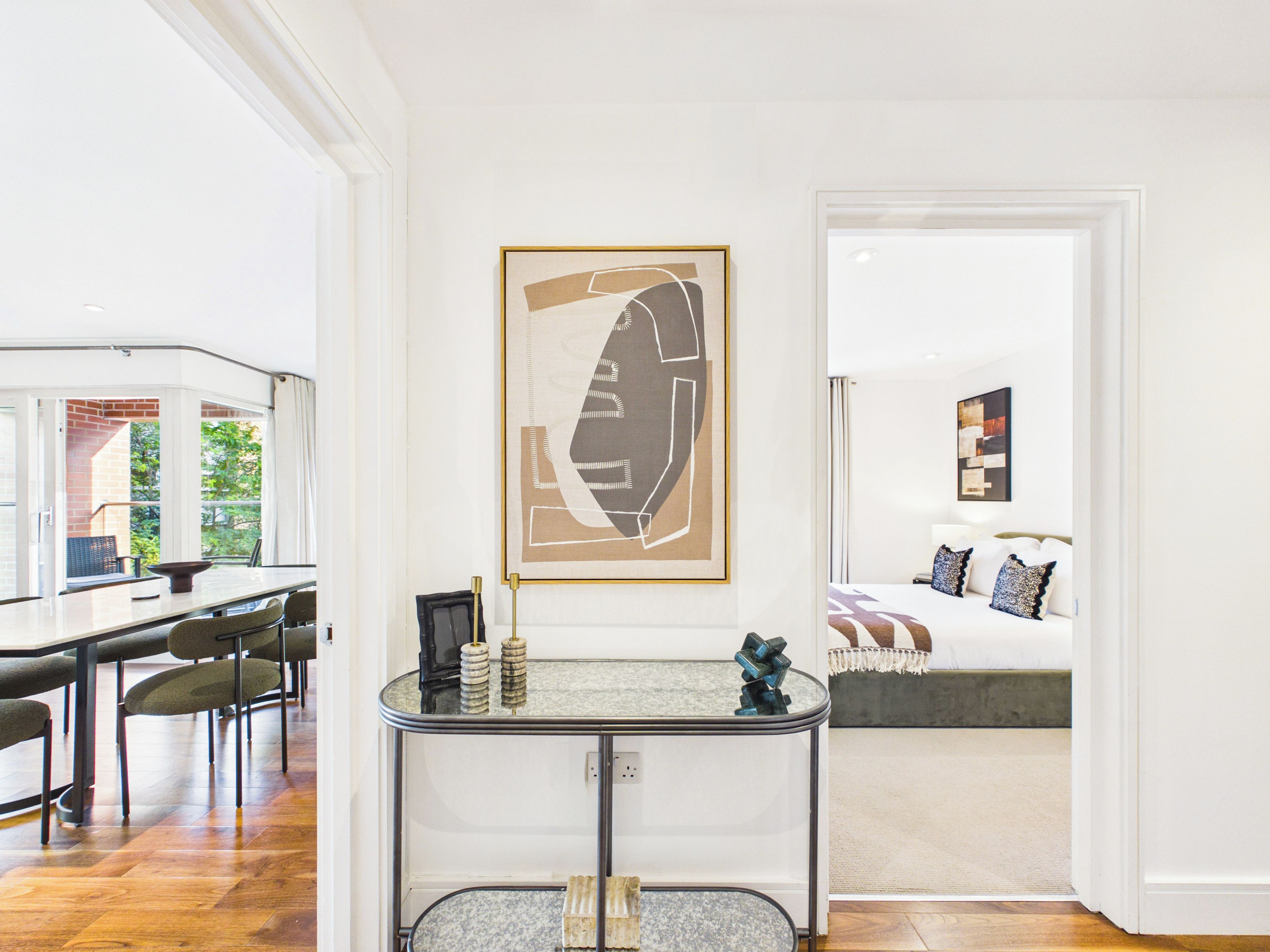 Interior moderno com área de jantar, mesa de vidro e objetos decorativos, e quarto com cama e almofadas.