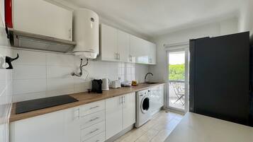 Uma cozinha moderna com armários brancos, máquina de lavar embutida e vista para o exterior.