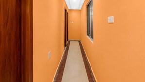 Um corredor com paredes laranja, uma porta de madeira à esquerda e uma janela à direita.
