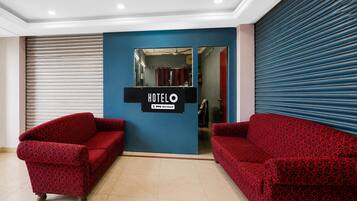Área de recepção de hotel com parede azul, um letreiro com a palavra 'HOTELO' e dois sofás vermelhos estampados.