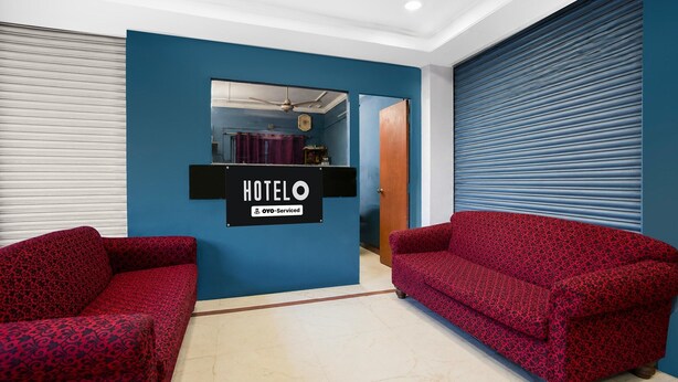 Recepção de hotel com parede azul, balcão de atendimento e dois sofás estampados vermelhos.