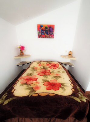 Quarto com colcha florida, um quadro na parede e duas mesas de cabeceira com objetos decorativos.
