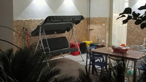 Uma área de pátio com balanço, mesa e cadeiras, e um muro de pedra.