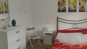 Um quarto com cama, cômoda, cadeira e obras de arte nas paredes.