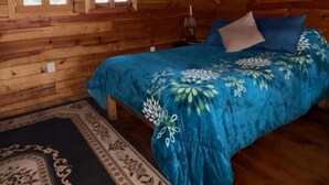 Quarto de cabana de madeira com cama, janela e tapete.