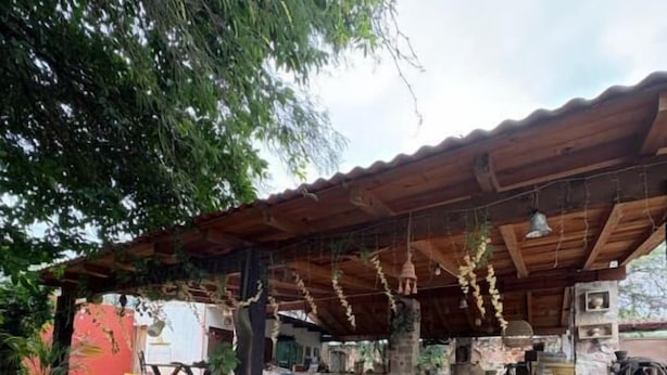 Um pátio externo com paredes de pedra, móveis de madeira e decorações penduradas.