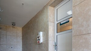 Um corredor com paredes e chão em azulejo, uma porta fechada com uma placa acima dela, e uma luminária no teto.