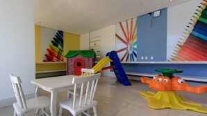 Uma área de recreação infantil com escorrega, estrutura de escalada e mesa com cadeiras.