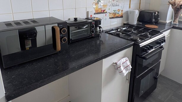 Uma cozinha moderna com bancada preta, forno embutido, fogão e torradeira.