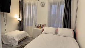 Quarto de hotel com duas camas, uma mesa de cabeceira, um abajur, um relógio e um quadro com pontos turísticos de Londres.