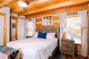 Quarto com painéis de madeira, uma cama grande, mesas de cabeceira e uma janela com cortinas.