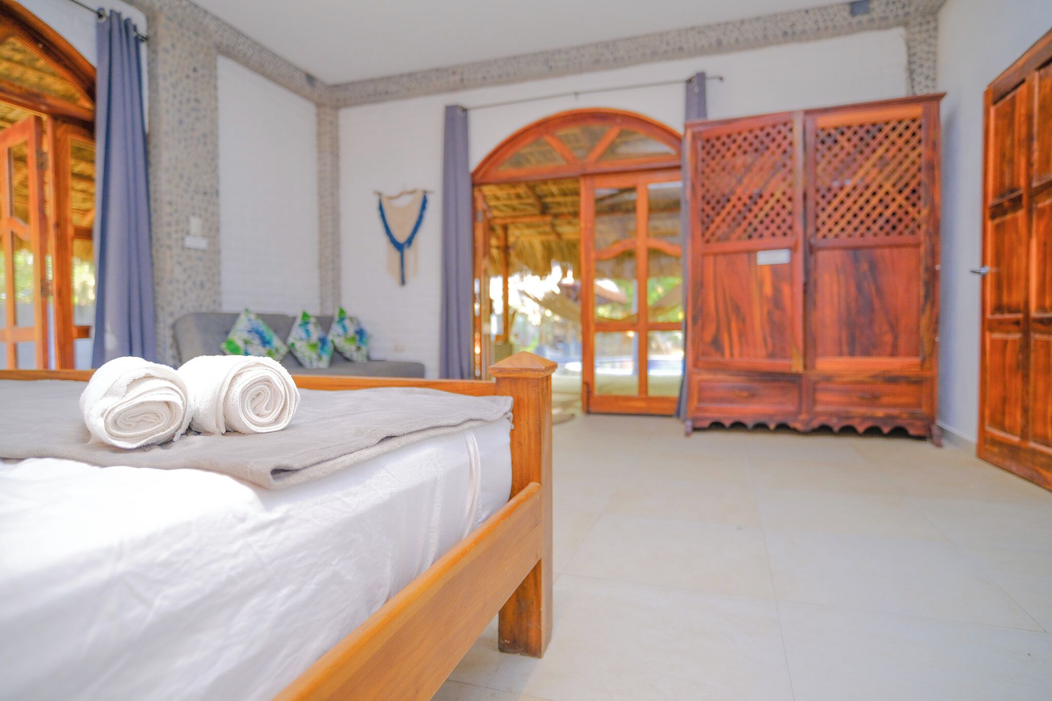 Quarto de hotel com cama, toalhas, cabeceira de madeira, uma janela grande e uma porta de madeira tradicional.