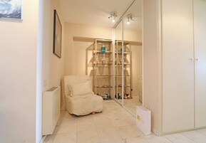 Um quarto com uma cadeira branca, um armário de vidro com prateleiras e uma porta branca.