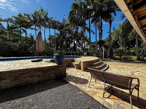 Uma área de piscina com um terraço de tijolos, uma espreguiçadeira e um vaso grande.