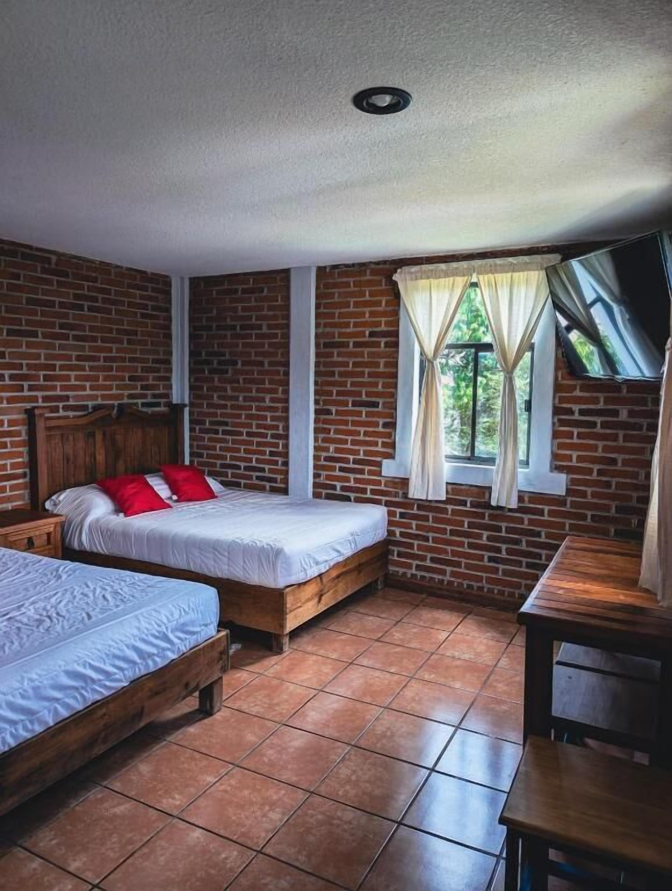 Quarto com duas camas, uma mesa de madeira e uma janela com cortinas.