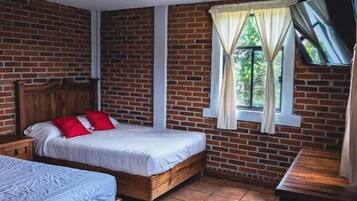 Quarto com duas camas, uma mesa de madeira e uma janela com cortinas.