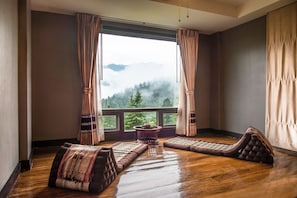 Quarto com uma janela ampla, piso de madeira e um sofá tradicional de palha.
