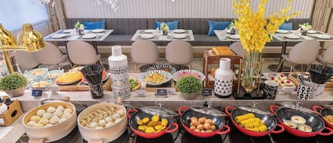 Disposição de buffet com diversos alimentos e estações de cozinha.