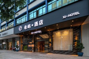 Um hotel com fachada moderna, grandes janelas e uma placa de destaque para 'XI HOTEL'.
