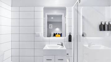 Um banheiro moderno com azulejos brancos, pia, espelho e área de chuveiro.