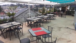 Um pátio externo com mesas e cadeiras, uma área coberta e vista para a cidade.
