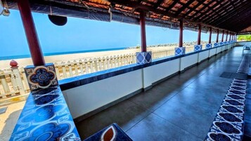 Uma galeria coberta com vista para a praia, com grade decorativa e piso de azulejos.