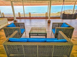 Uma área de estar coberta ao ar livre, com móveis de vime e vista para o mar.