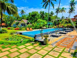 Área de piscina com piscina azul cristalina, rodeada por palmeiras e um jardim bem cuidado.