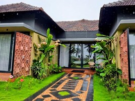 Uma casa moderna com telhado de telhas, um caminho pavimentado que leva à entrada e vegetação exuberante.