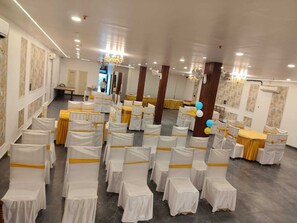Uma sala de banquetes com fileiras de mesas e cadeiras, lustres e painéis decorativos na parede.