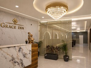Uma área de recepção de hotel com balcão de mármore, um candelabro e uma estátua decorativa de Buda.