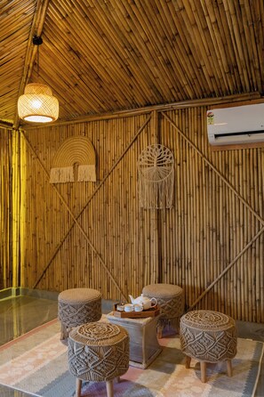 Quarto com teto de bambu, luminária pendente, tapeçaria de macramé e uma pequena mesa com bandeja de chá e xícaras.