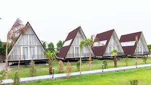 Uma fileira de cabanas com telhados triangulares, um gramado à frente e um caminho pavimentado.