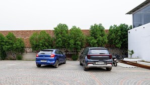 Dois carros estacionados num pátio com um muro de tijolos e vegetação ao fundo.