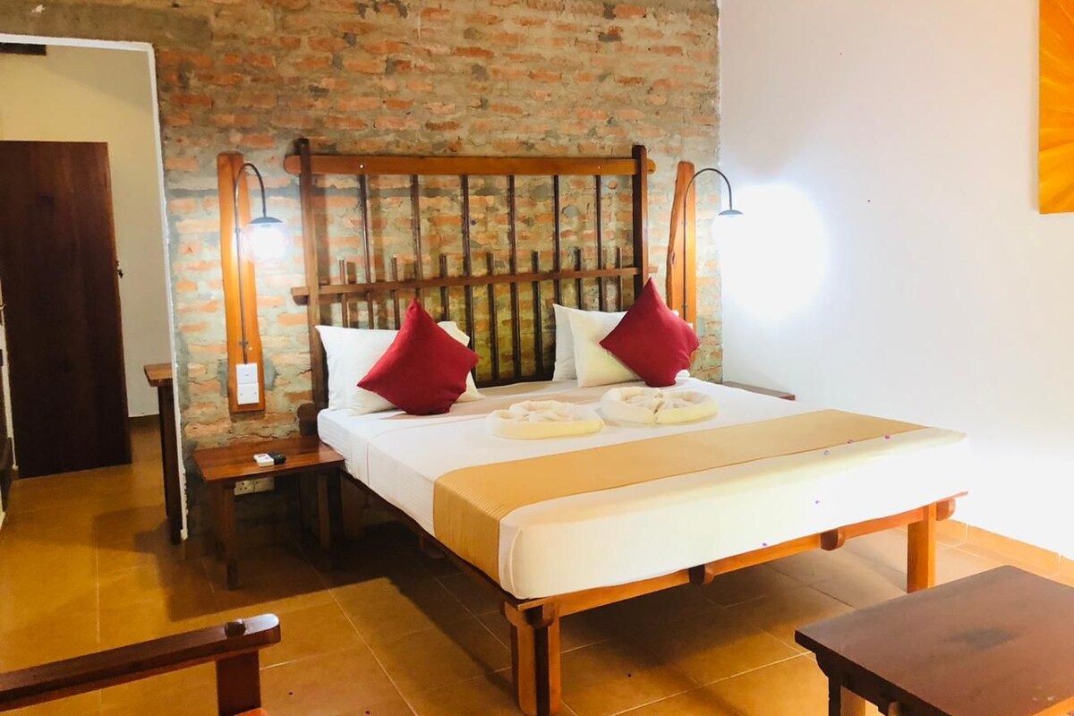 Quarto com parede de tijolos, cama de madeira com cabeceira, mesa de cabeceira e apoio para luminária.
