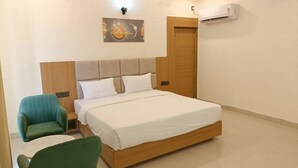 Quarto de hotel com uma cama, duas cadeiras, ar condicionado fixado na parede e uma porta.