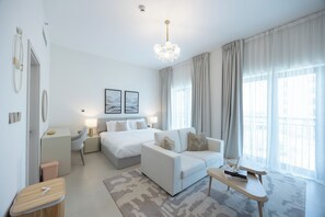 Quarto de hotel moderno com cama, sofá, escrivaninha e uma grande janela com cortinas.