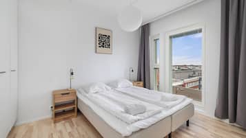 Quarto moderno com uma cama grande, mesas de cabeceira, luminária pendente e vista da cidade através de uma janela ampla.